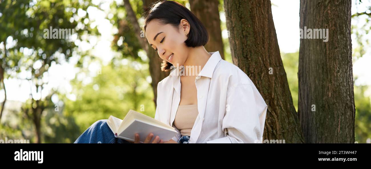 Beautiful smiling girl reading book in park on sunny day, sitting near ...
