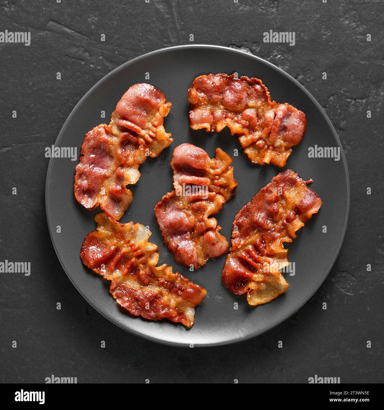 Roasted bacon on plate over black stone background. Top view, flat lay ...