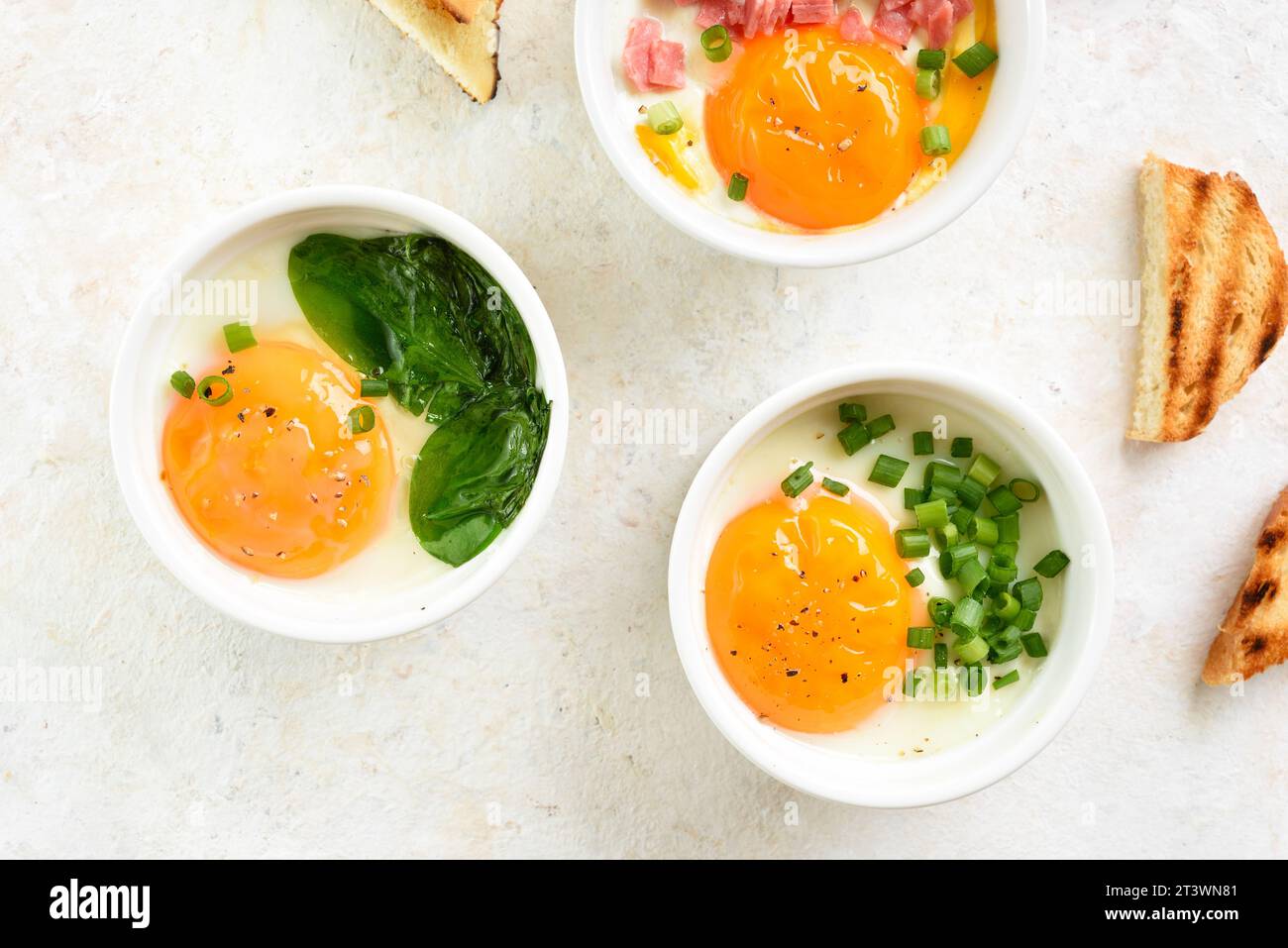 Eggs en cocotte (baked eggs) in ceramic bowls over light background ...