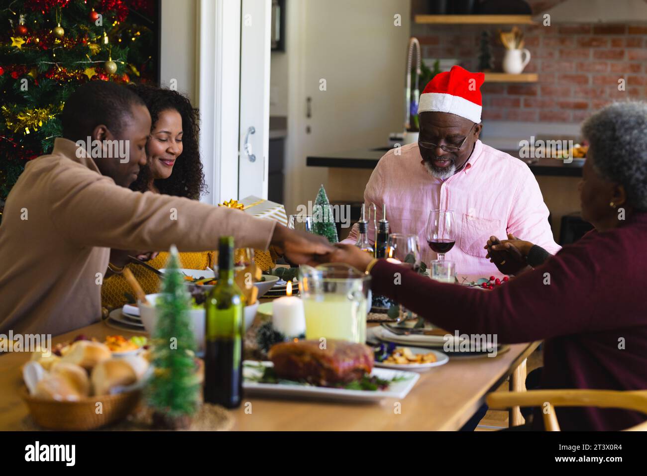 Happy african american family praying before christmas dinner in decorated dining room at home ...