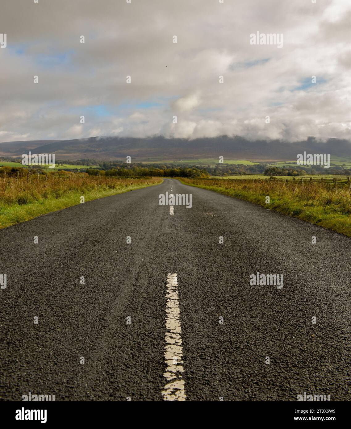 A straight bit of tarmac road through countryside with distant fells ...