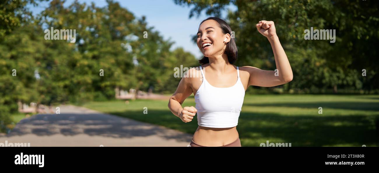 Happy fitness girl achieve goal, finish marathon, running with hands up ...