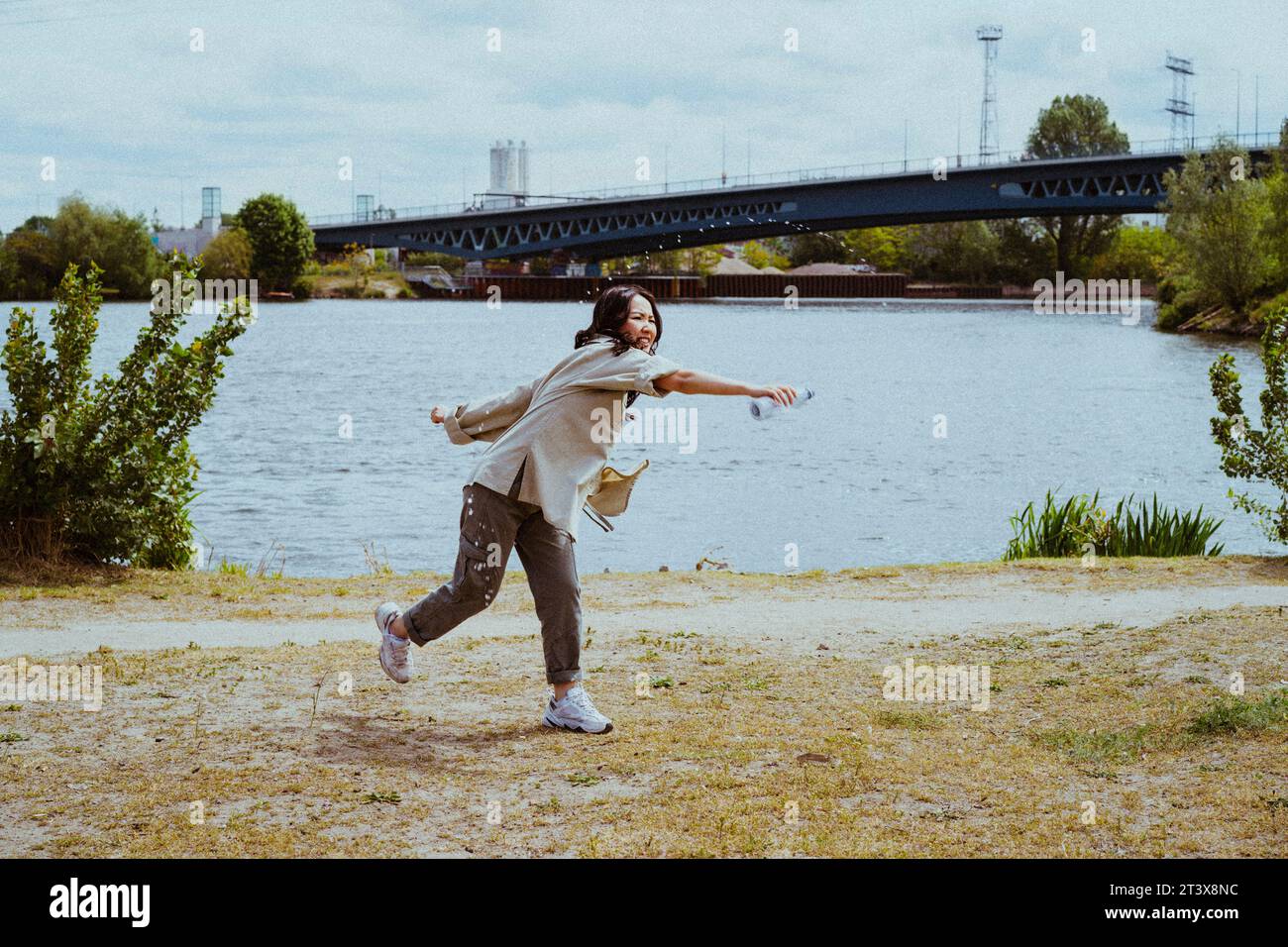 Full length of young woman throwing water from bottle near river Stock ...