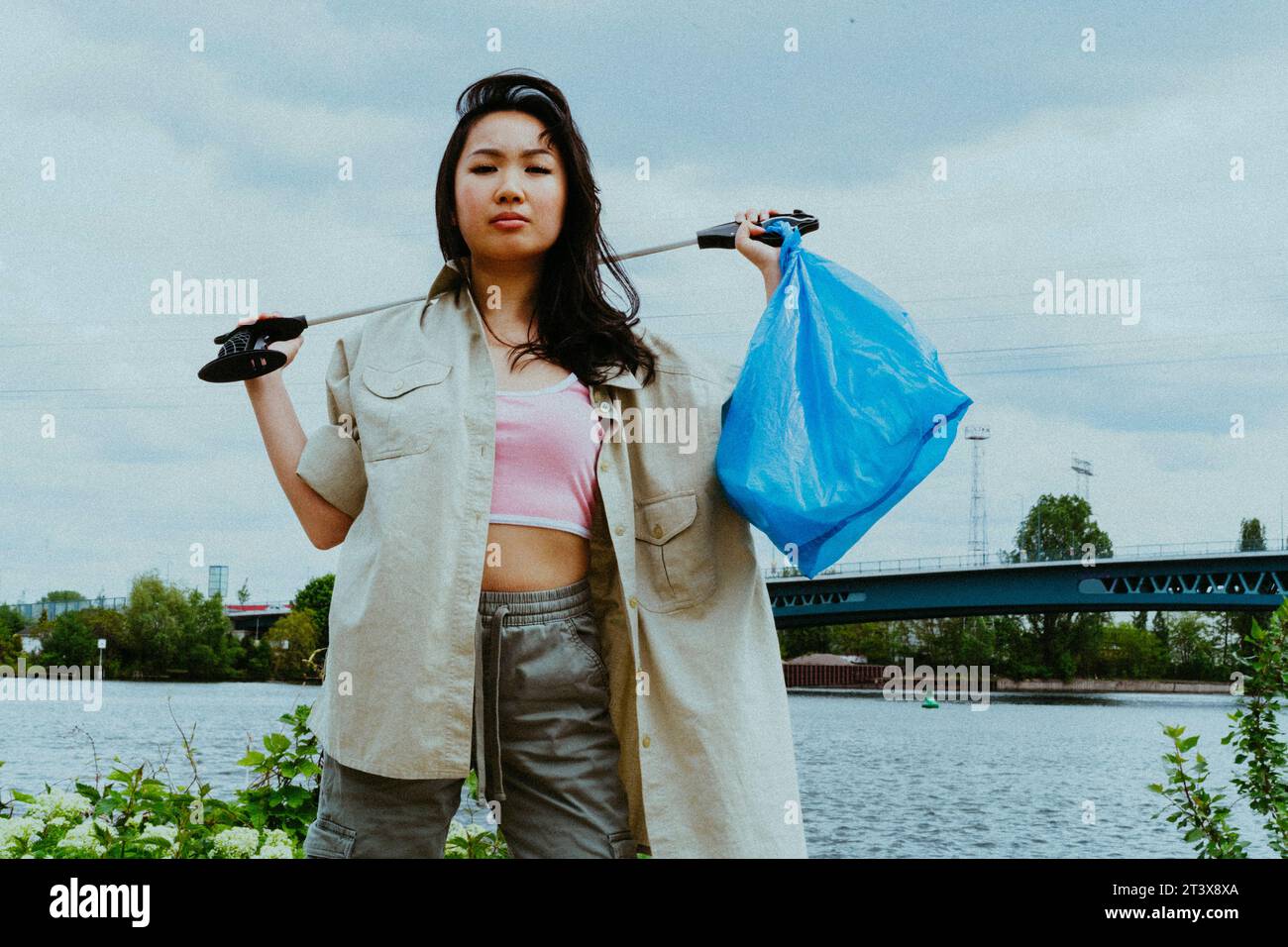 Low angle portrait of confident young woman picking garbage near river ...