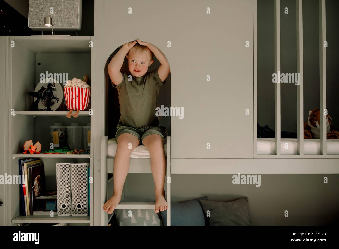 Full length of boy with down syndrome sitting on bunkbed ladder at home ...