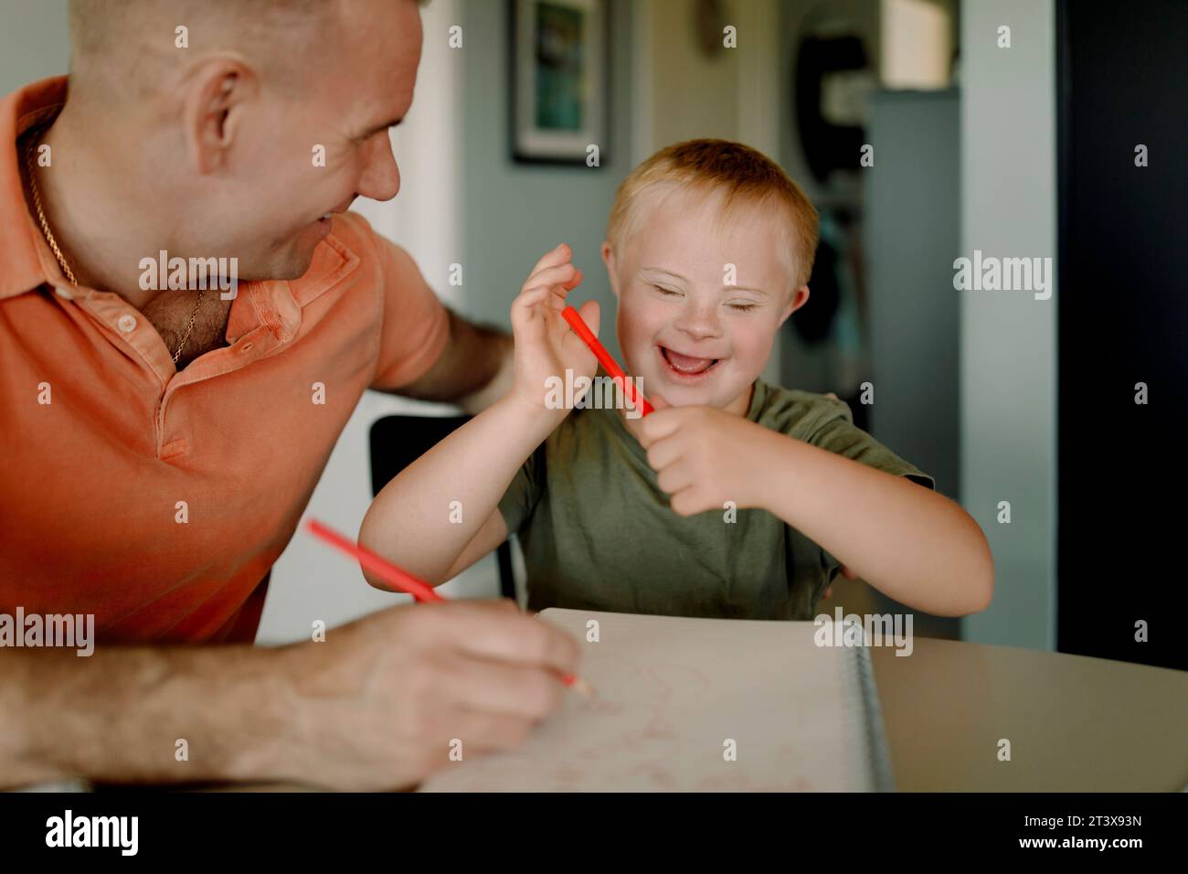 Happy father and son with down syndrome drawing in book at dining table ...