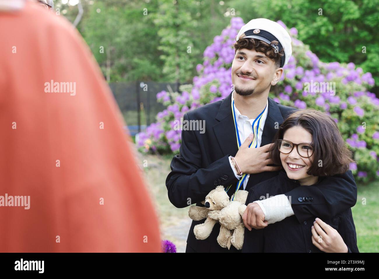 Smiling young man with arm around boy looking at woman in back yard ...