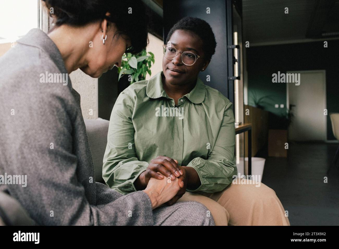Businesswoman consoling mature female colleague while holding hands at ...