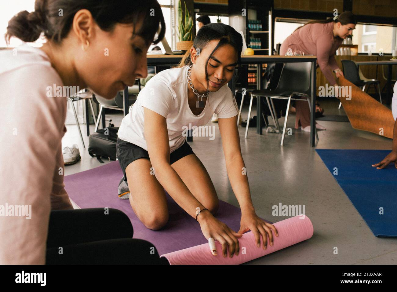 Non-binary business person rolling exercise mat by colleague at office ...