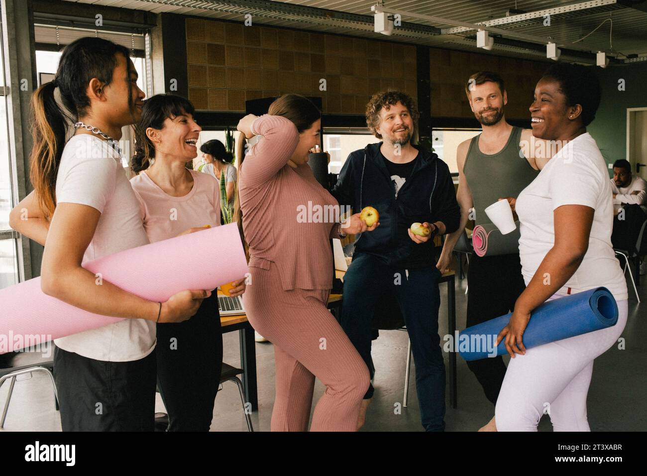 Happy multiracial colleagues standing with yoga mats and fruits in ...