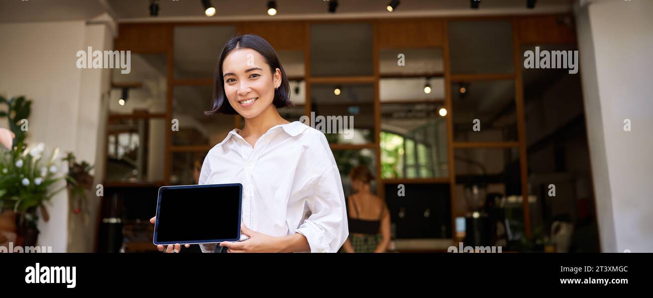 Smiling asian female manager, cafe owner, showing tablet screen ...