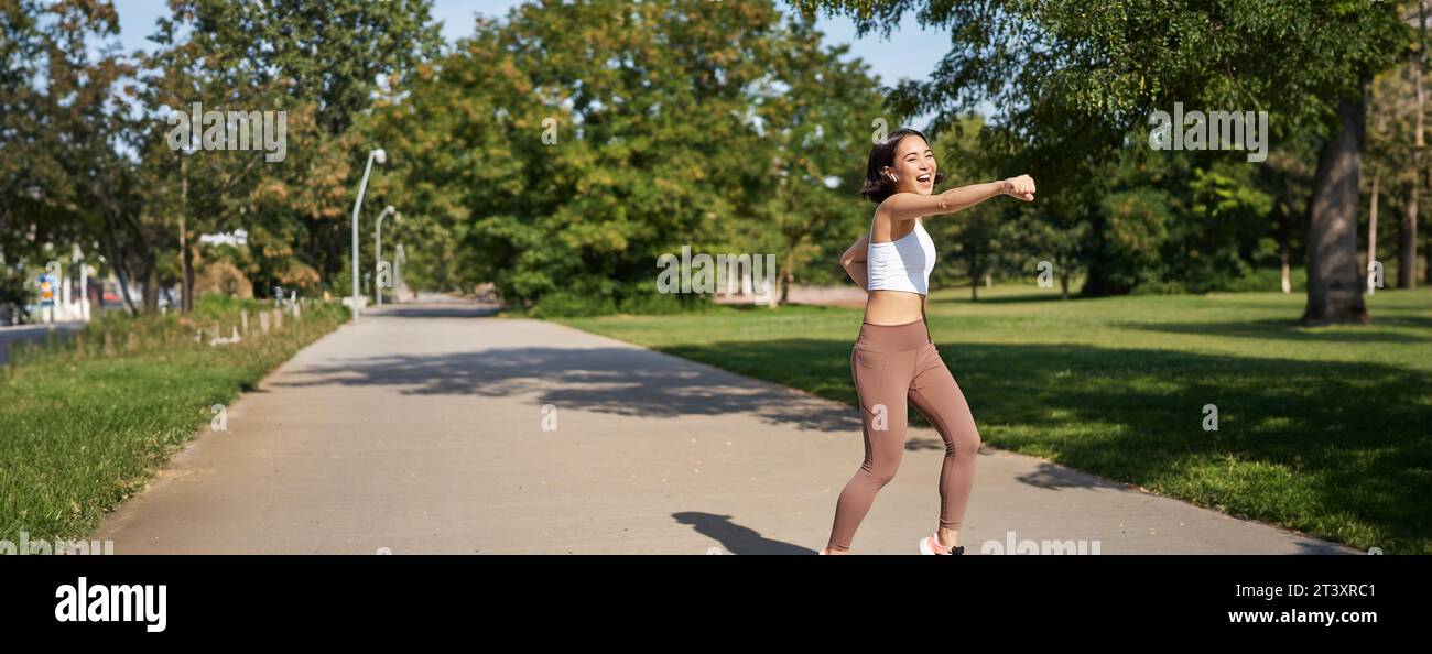 Excited young asian woman winning, finish running in park, saying yes ...
