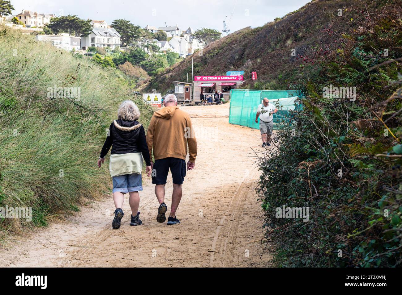 A couple walking along a sandy track to Crantock Beach in Newquay in ...