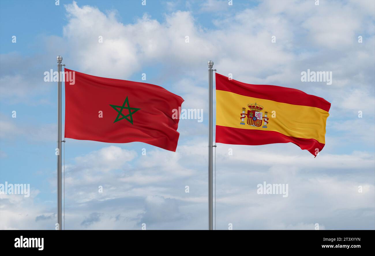 Spain and Morocco flags waving together in the wind on blue cloudy sky ...