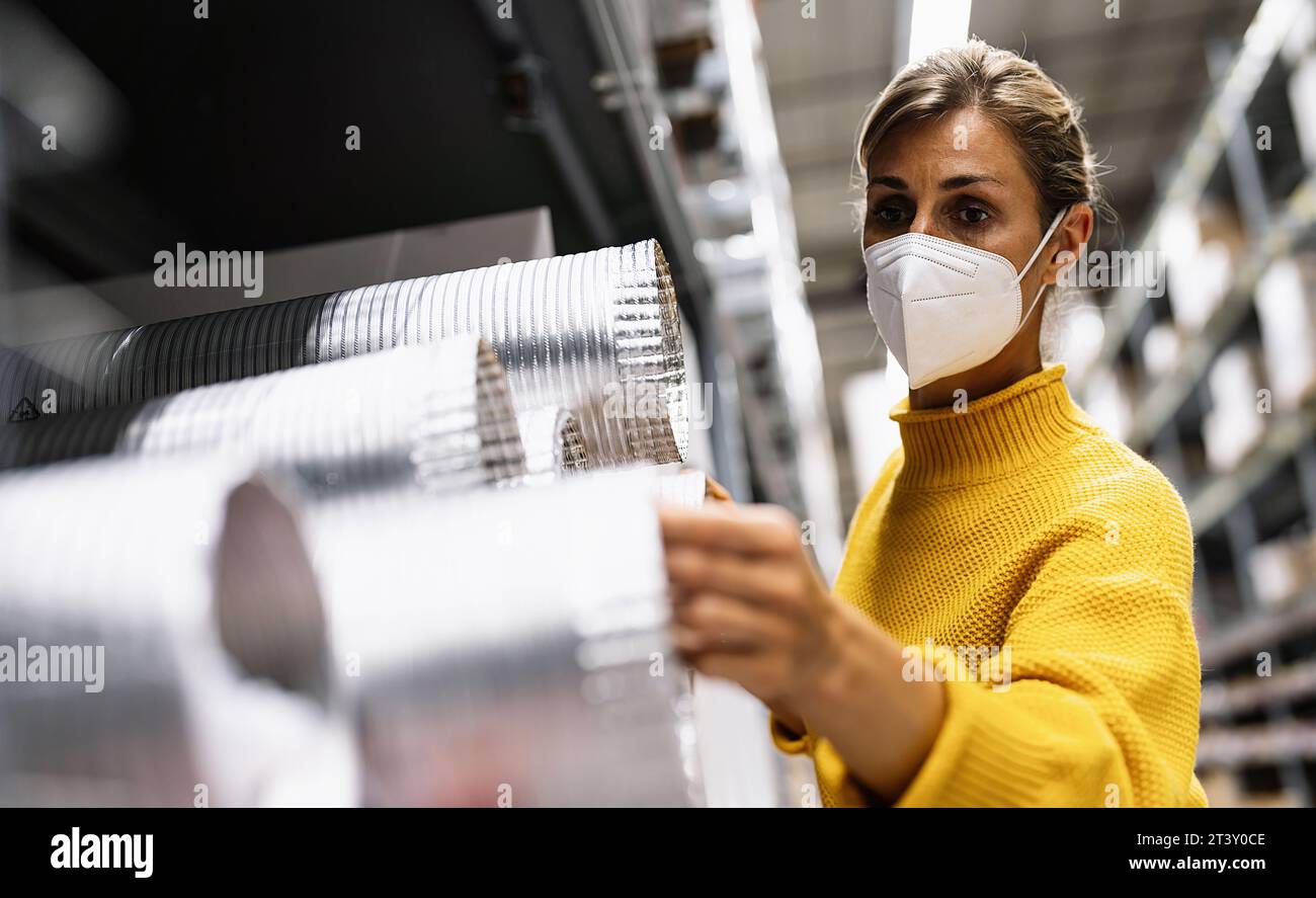 woman with face mask examines silver ventilation tubes in a warehouse ...