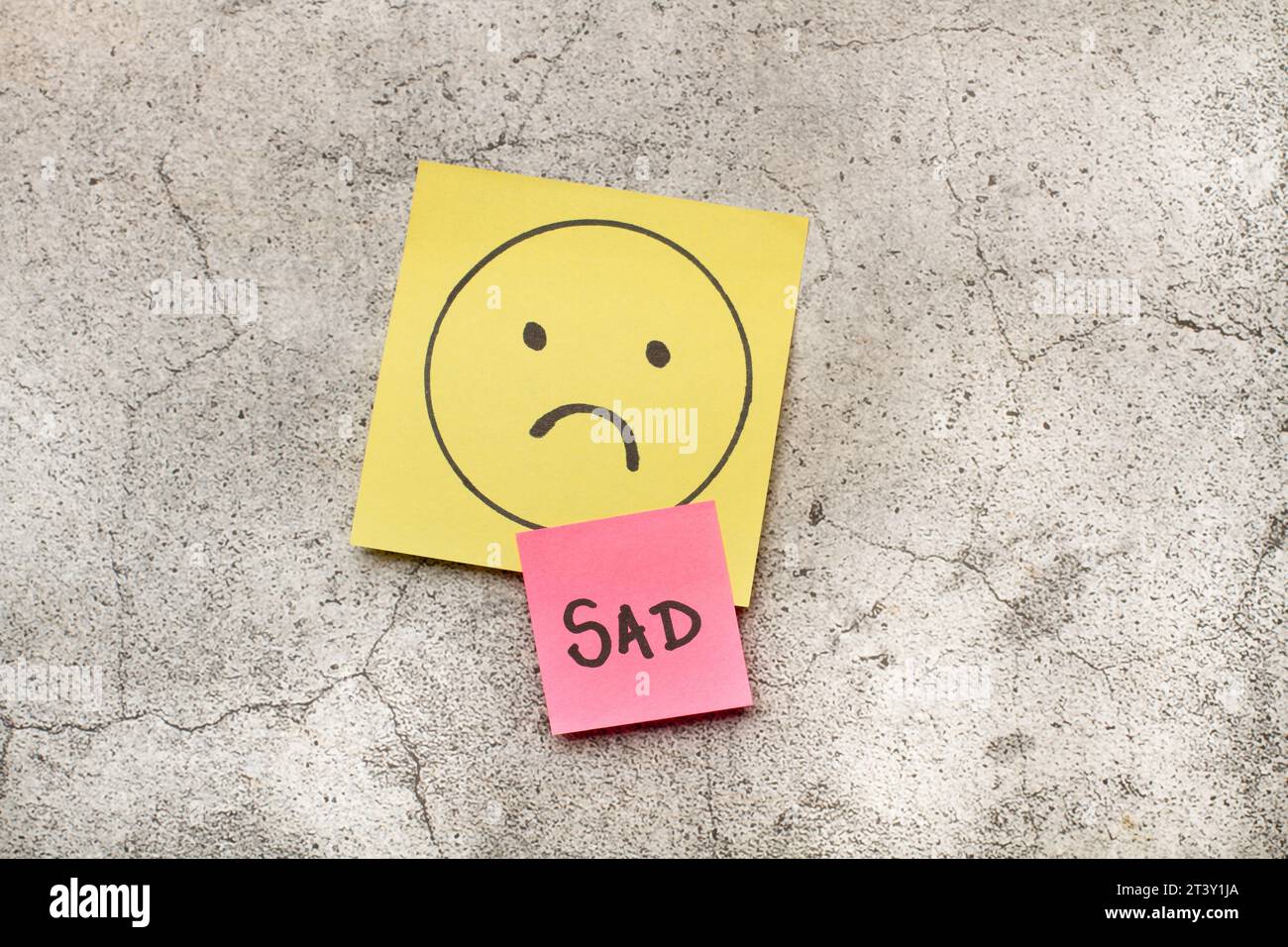 Colored paper notes with sad drawing face and single word on a gray ...