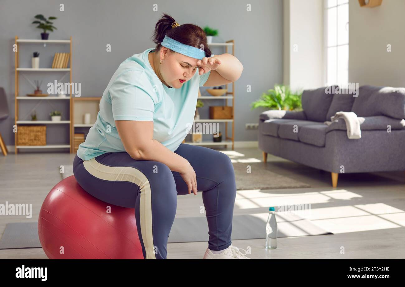 Fat woman, tired after workout, sitting on exercise ball and wiping ...
