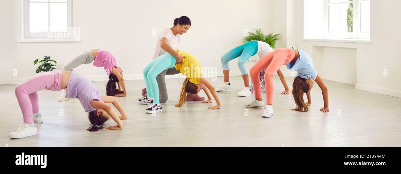 Woman trainer helps flexible children to do bridge exercise at ...