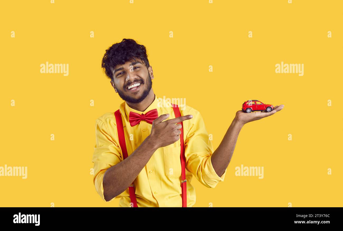 Cheerful Indian guy points his finger at small toy car in his hand ...