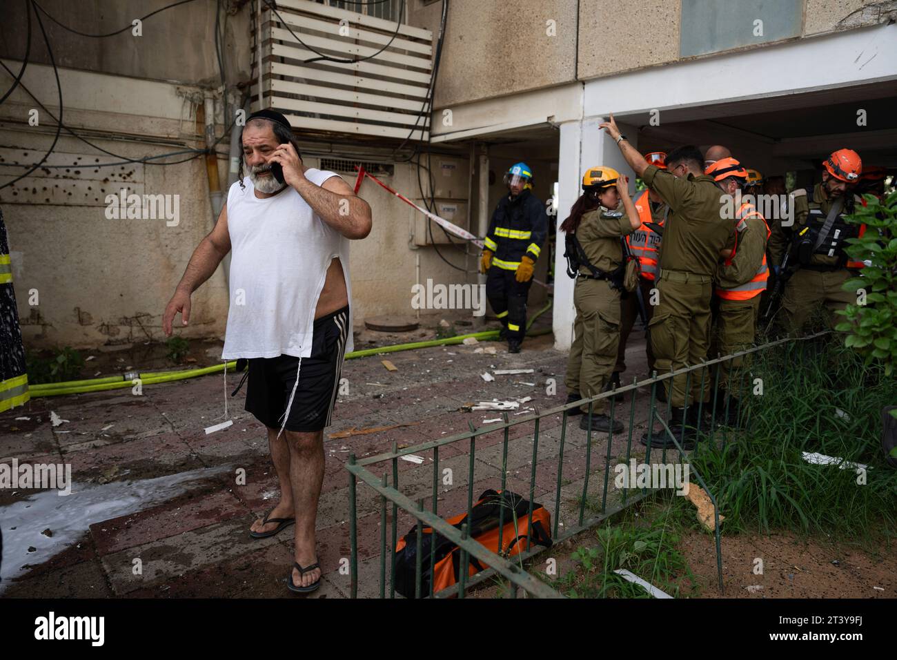 An Israeli man talks on his phone next to a building struck by a rocket ...