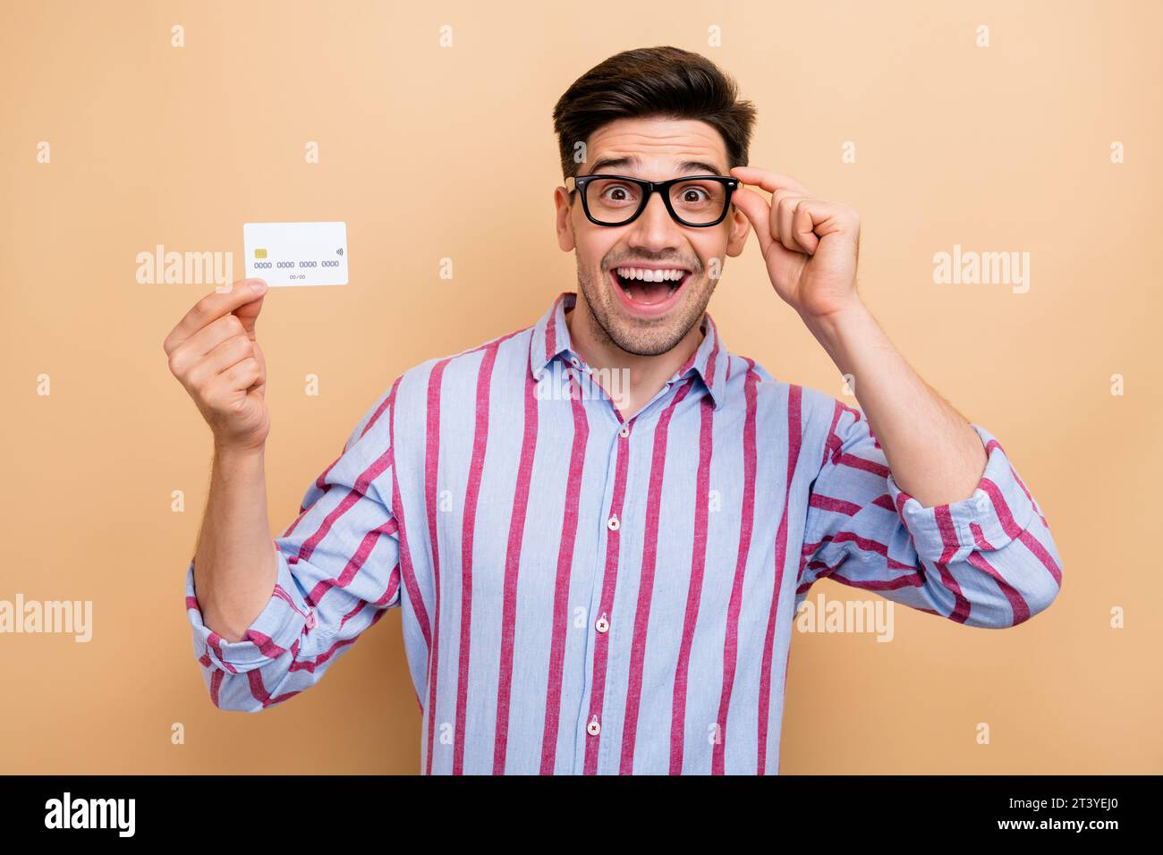 Photo of amazed funny guy wearing striped shirt holding plastic debit ...