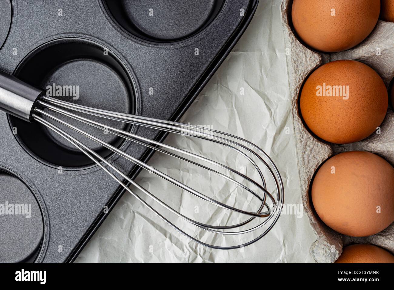 Form for baking cupcakes, eggs in a box and a whisk on a white ...