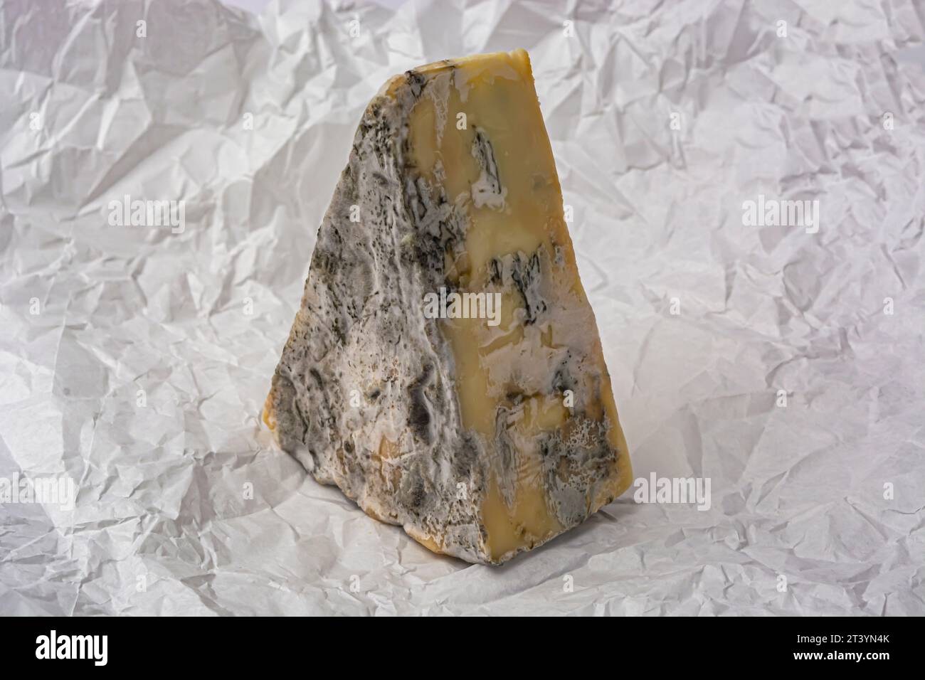 triangular piece of cheese with mold on white crumpled paper close-up ...
