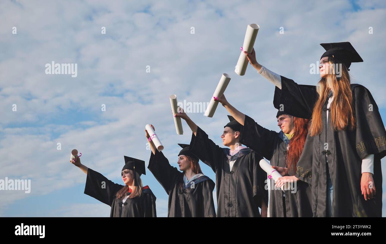 Cheerful graduates pose with raised diplomas on a sunny day Stock Photo ...
