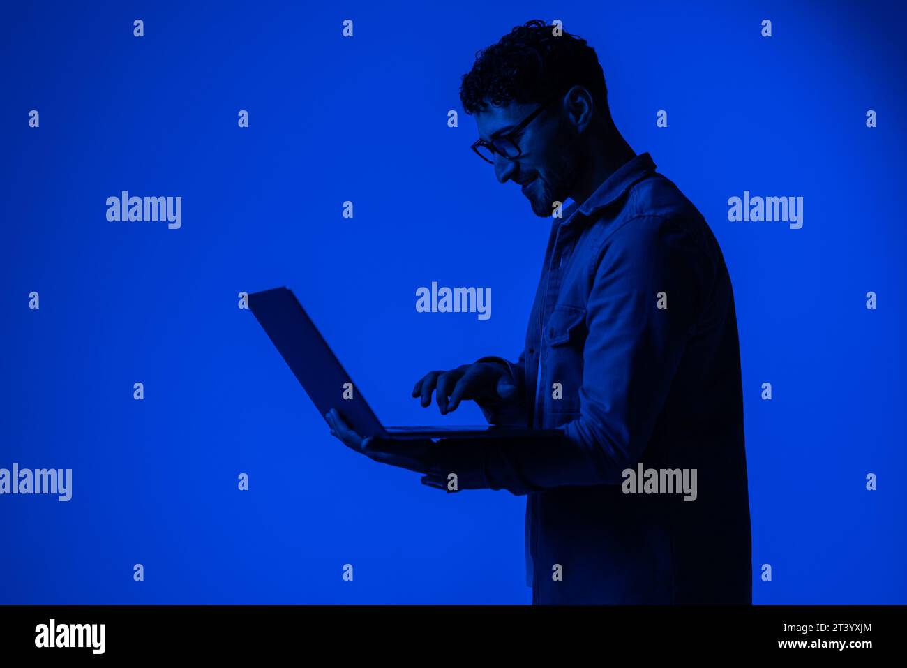 Using laptop. Caucasian man's portrait isolated on blue studio ...