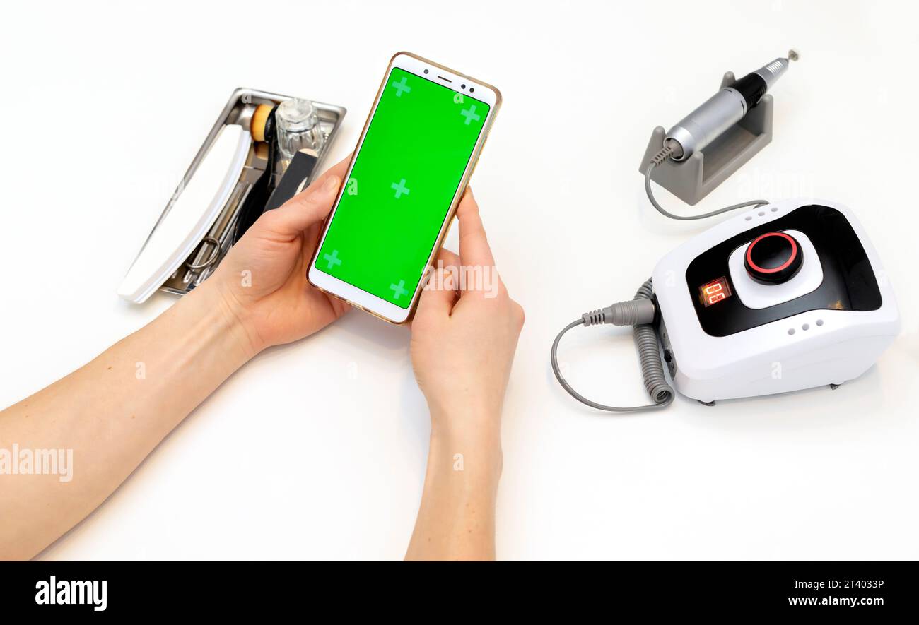 Nail stylist hands hold gadget with green chroma key screen, sitting at ...