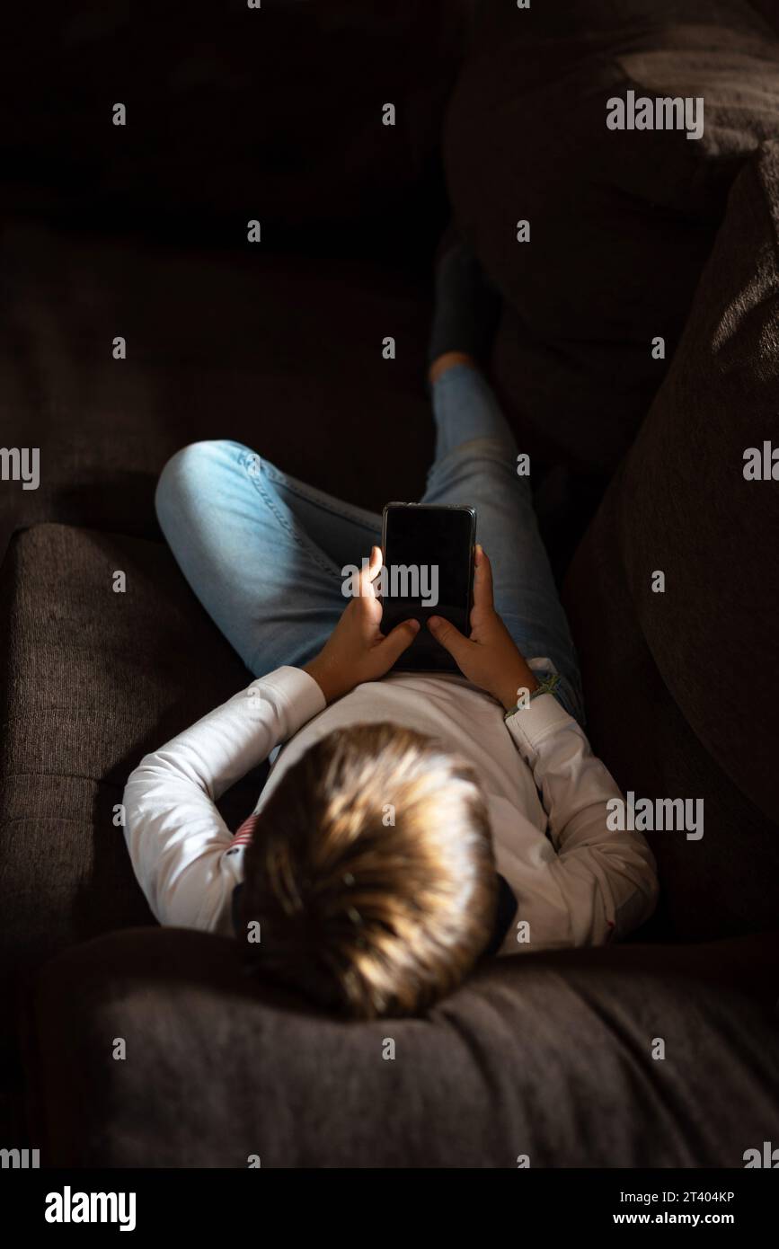 A child lying on the couch, staring at a mobile phone. Addiction and ...
