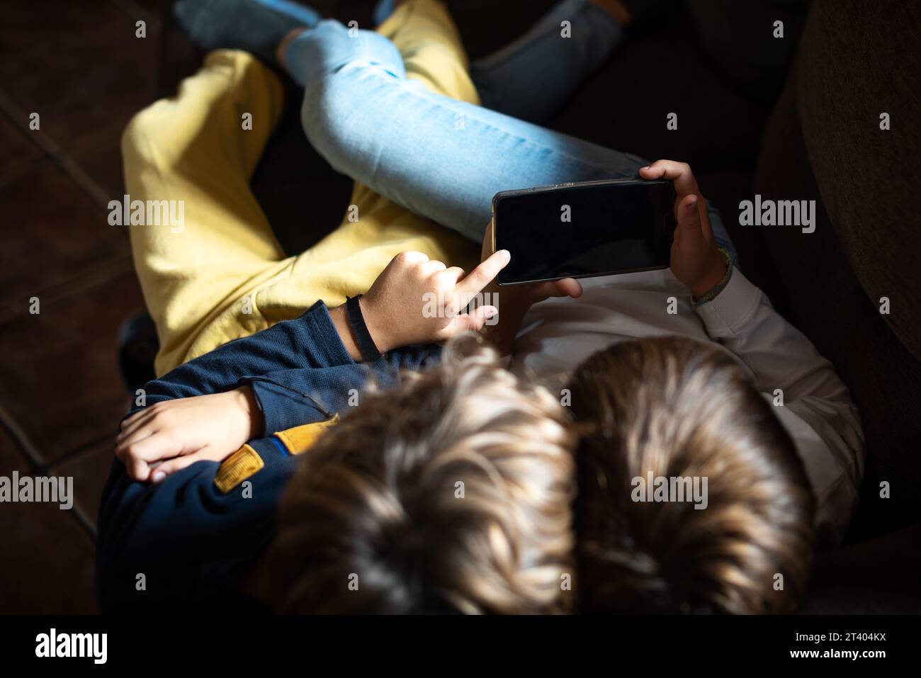 Two children lying on the couch, staring at a mobile phone. Addiction ...