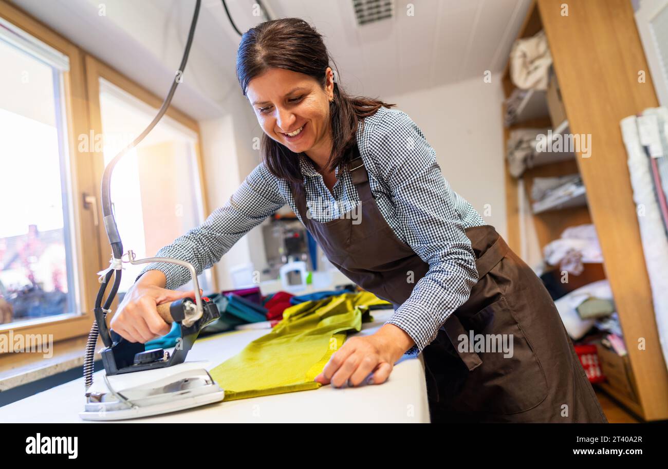 smiling woman is ironing a piece of vibrant green silk fabric in a well ...