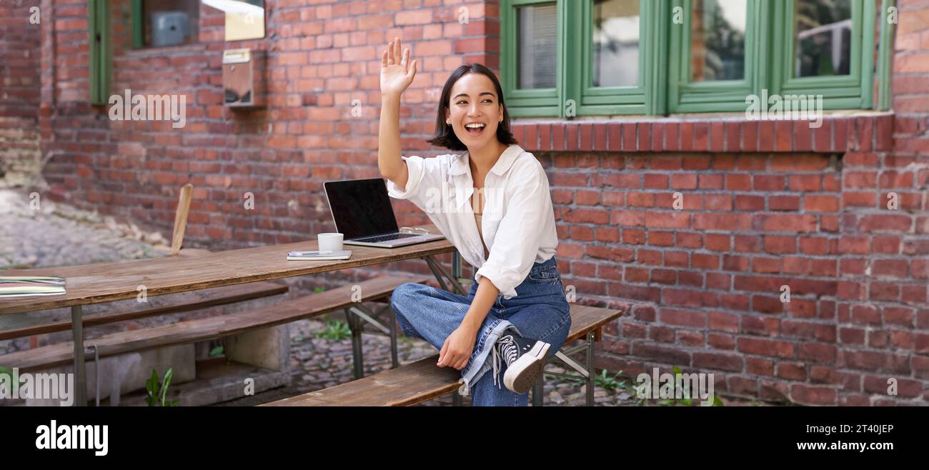 Vertical shot of happy girl attracting attention, waving hand at friend ...