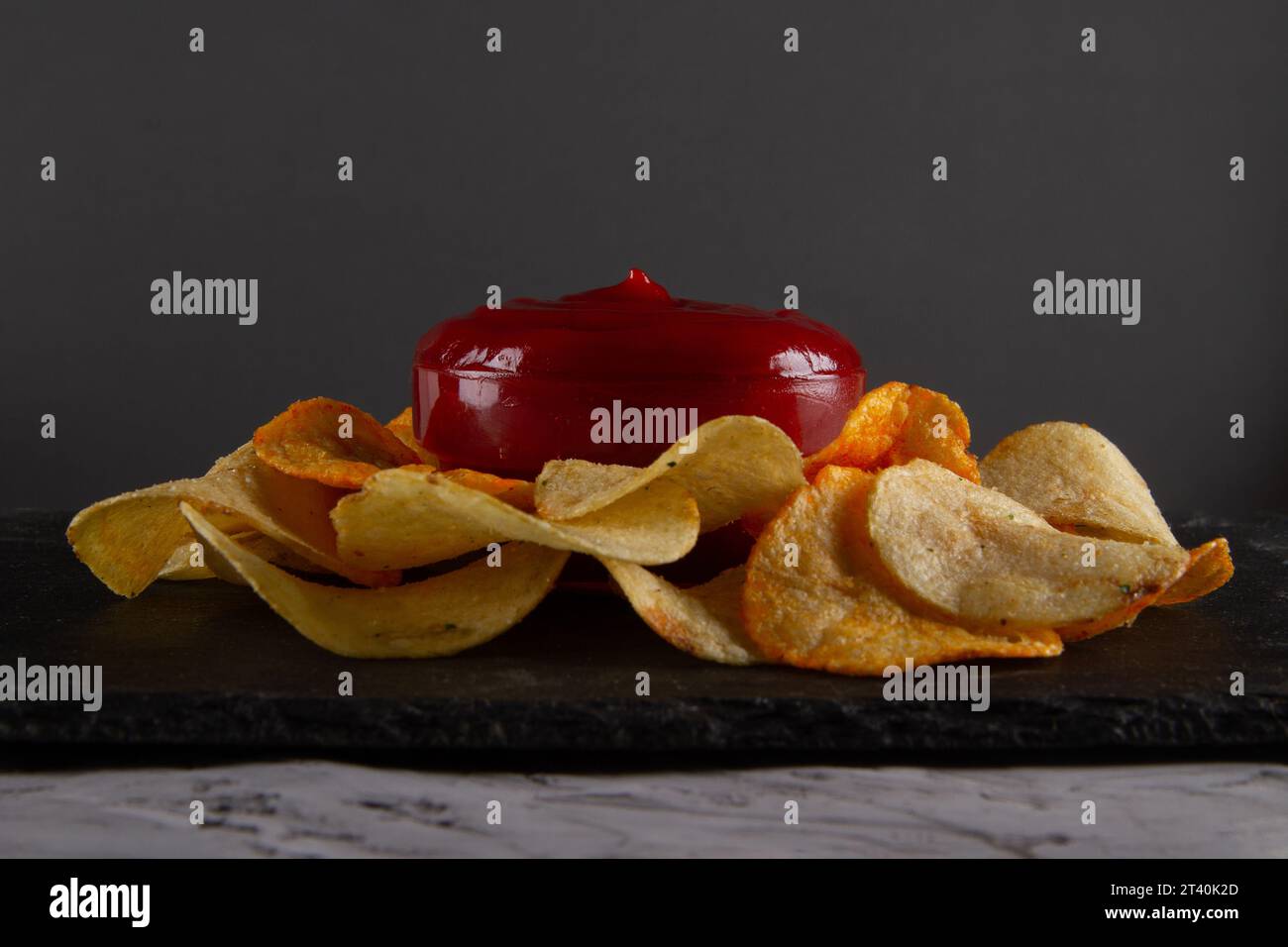 Side view of heap of potato chips with red dipping sauce on black slate ...
