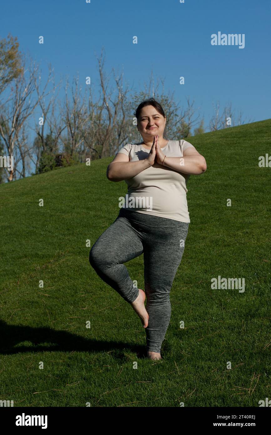 overweight middle-aged woman practices yoga outdoors barefoot, doing ...