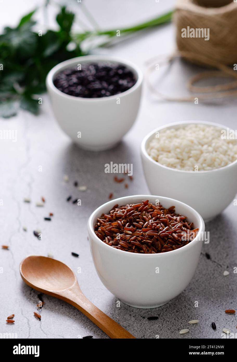 Red, black, and Yamani rice in white bowls, a wooden spoon and a rustic ...
