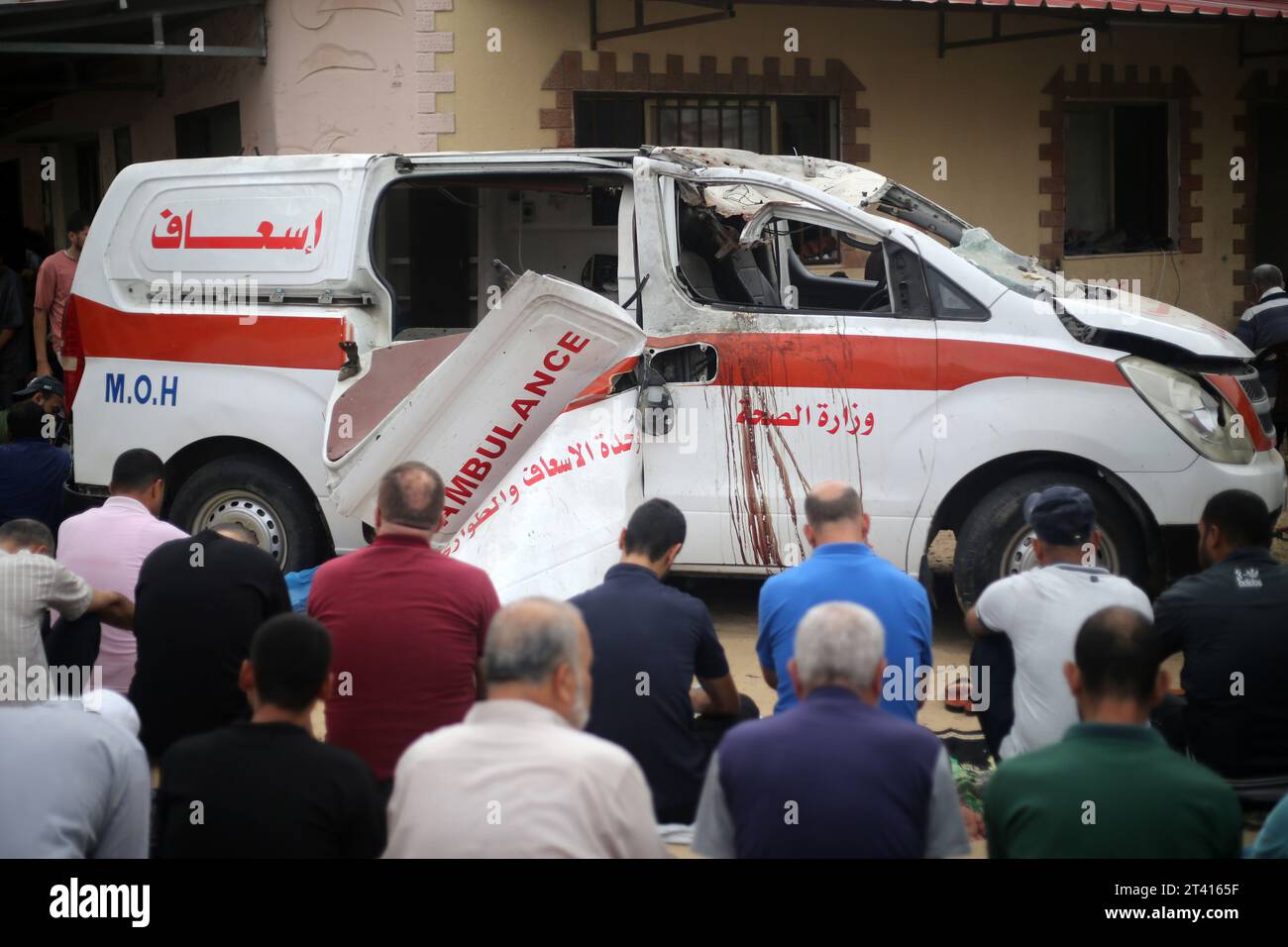 Palestinians, seated on the ground close to a damaged ambulance, take ...
