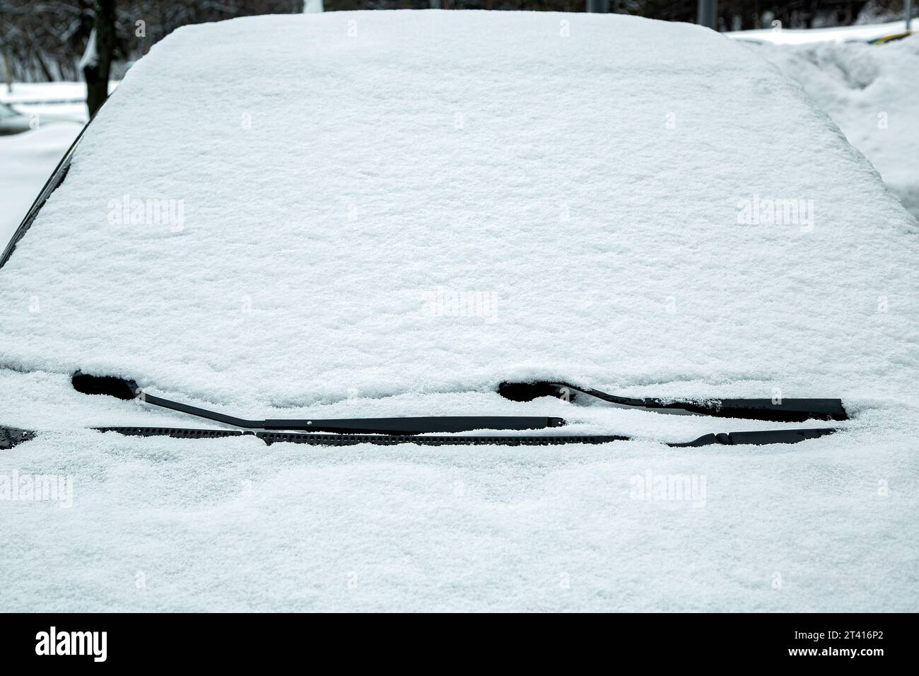 windshield with wipers of a snow-covered car in the early winter ...