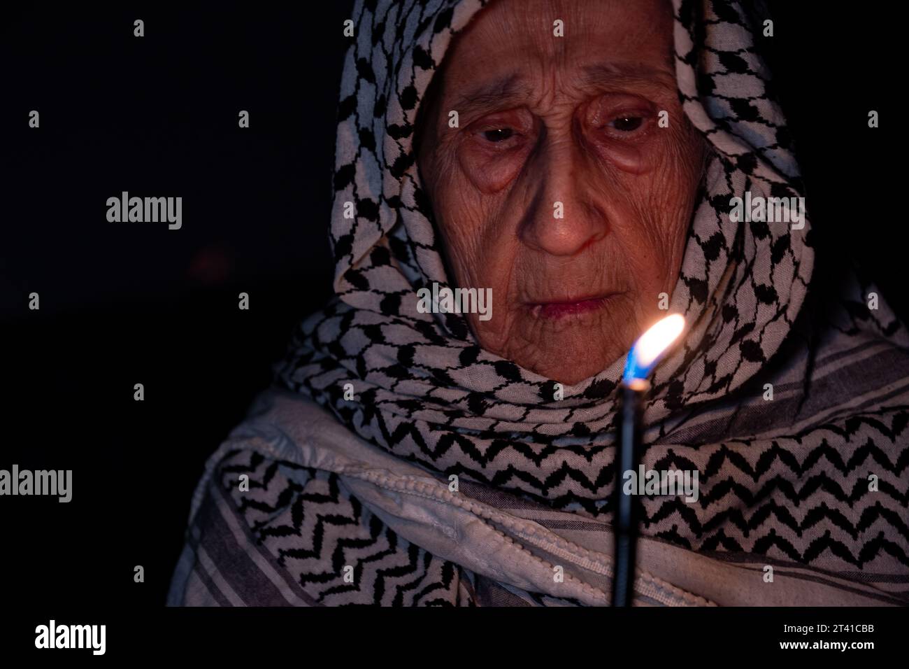 Portrait of old lady wearing white palestinian keffiyeh in dark holding ...