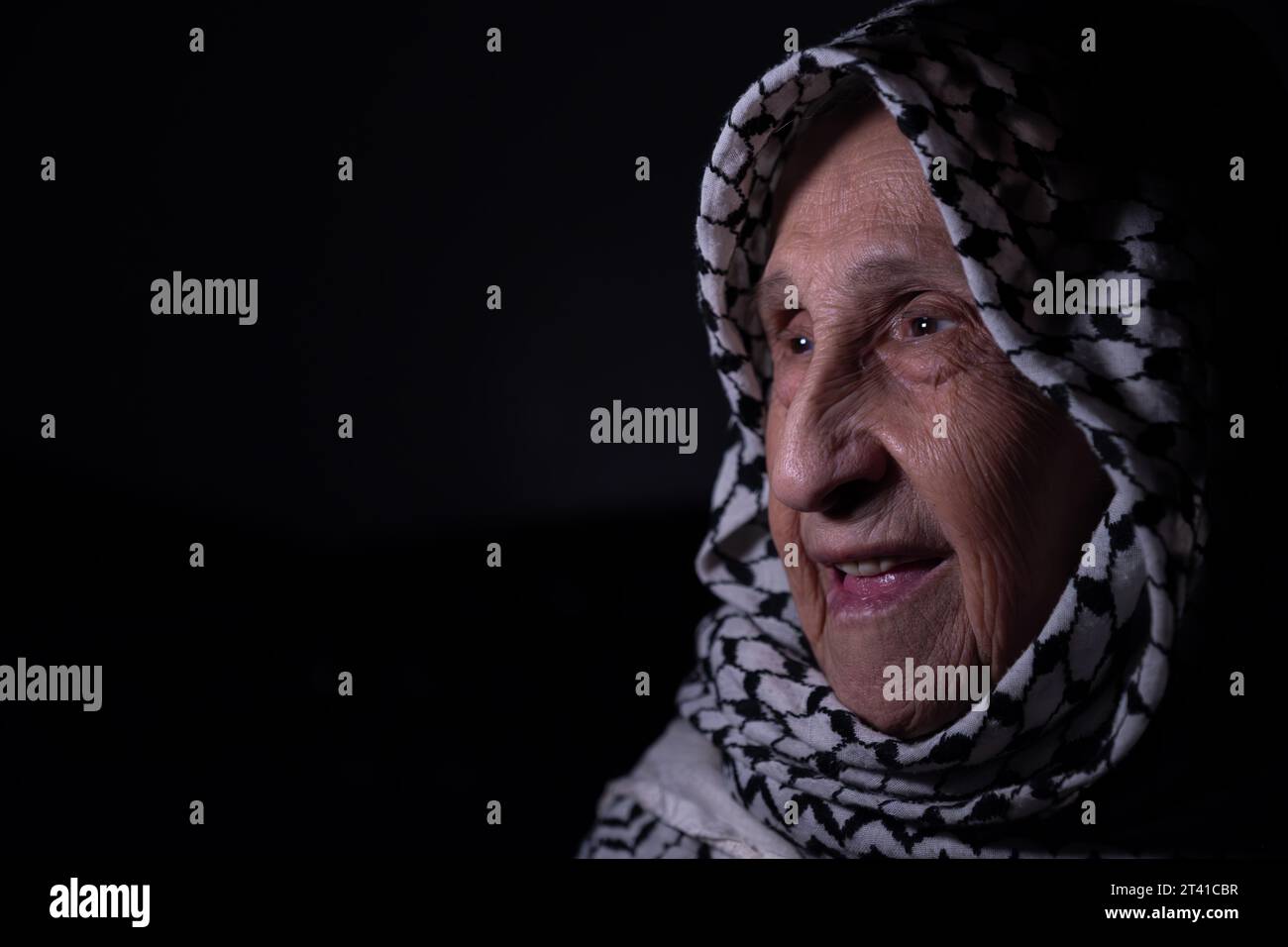 portrait of an old lady in dark background wearing white palestinian ...