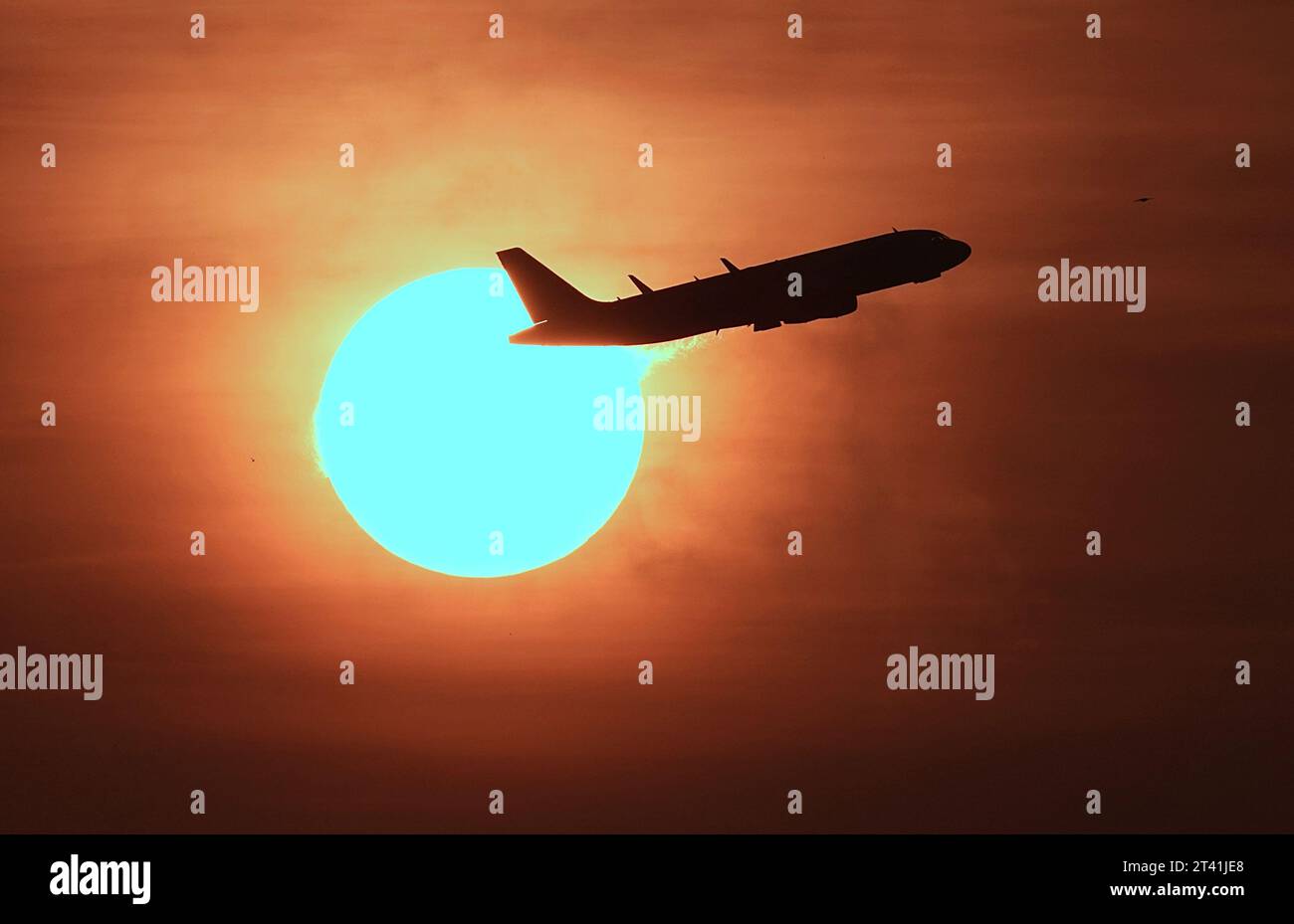 A medium-sized airplane flying in front of a vibrant orange and pink ...