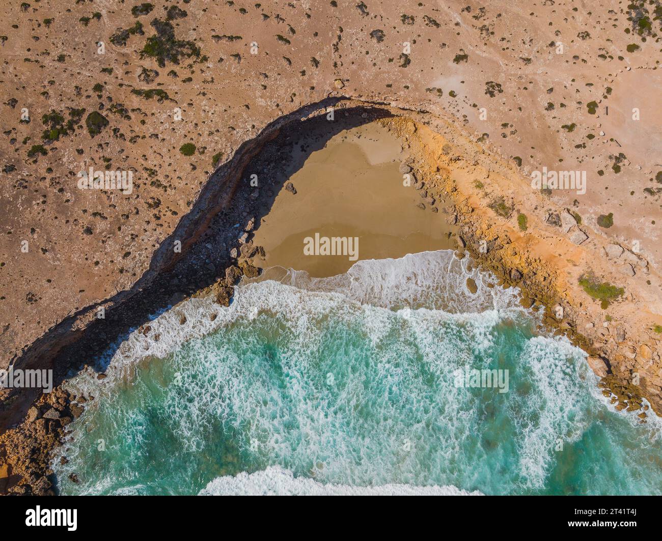 Aerial view of waves rolling into a small bay below an arid cliff top ...