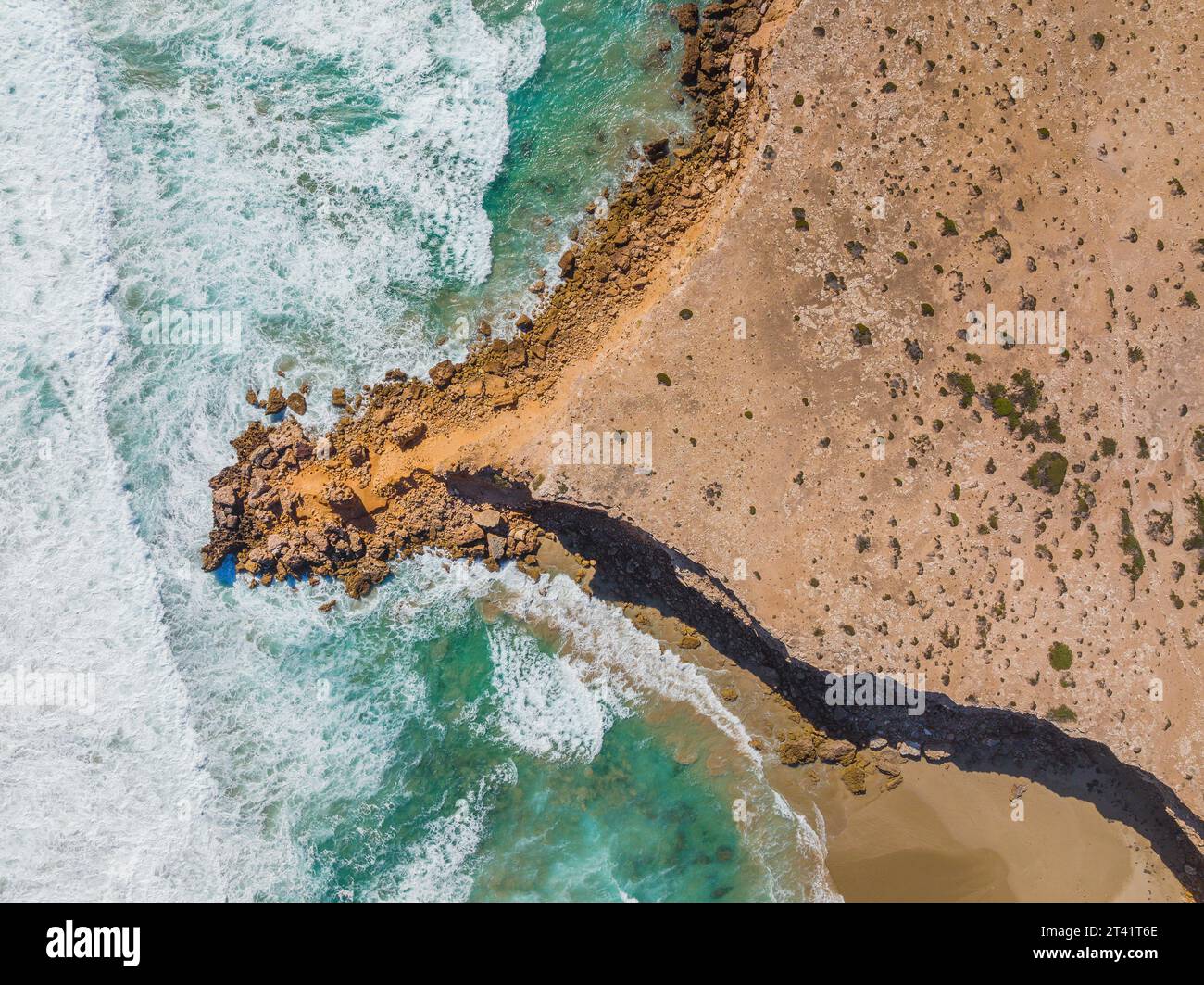 Aerial view of waves crashing onto a rocky point on the edge of an arid ...