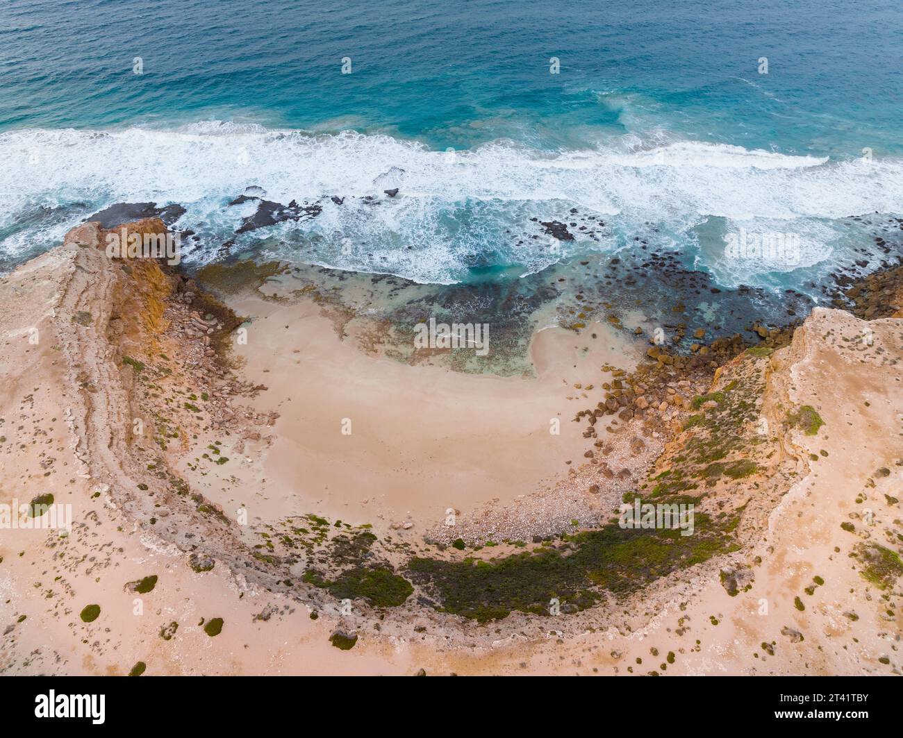 Aerial view of waves rolling into a small bay below an arid cliff top ...