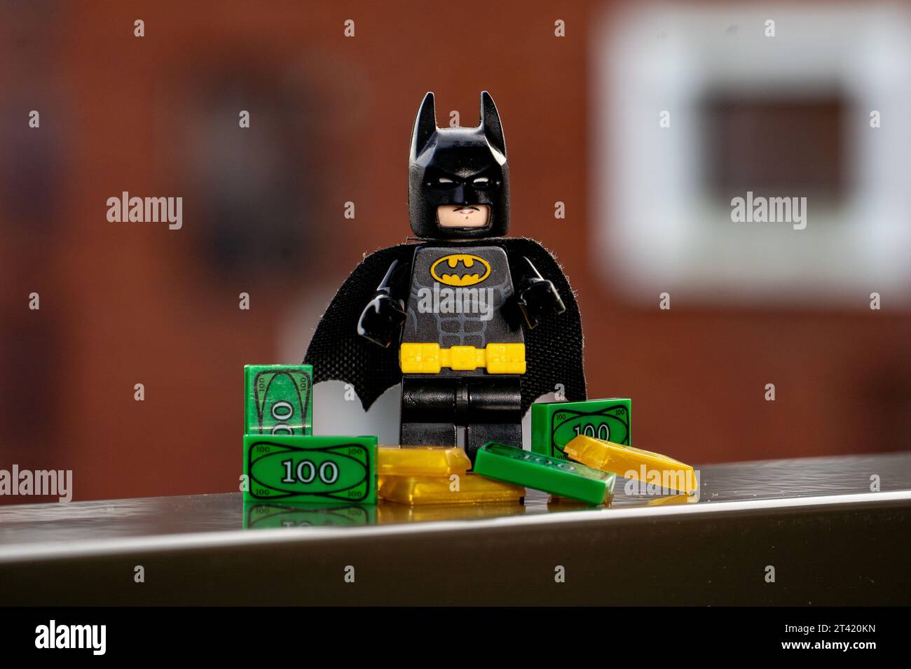 A Lego mini figure of Batman standing behind a pile of money and gold ...