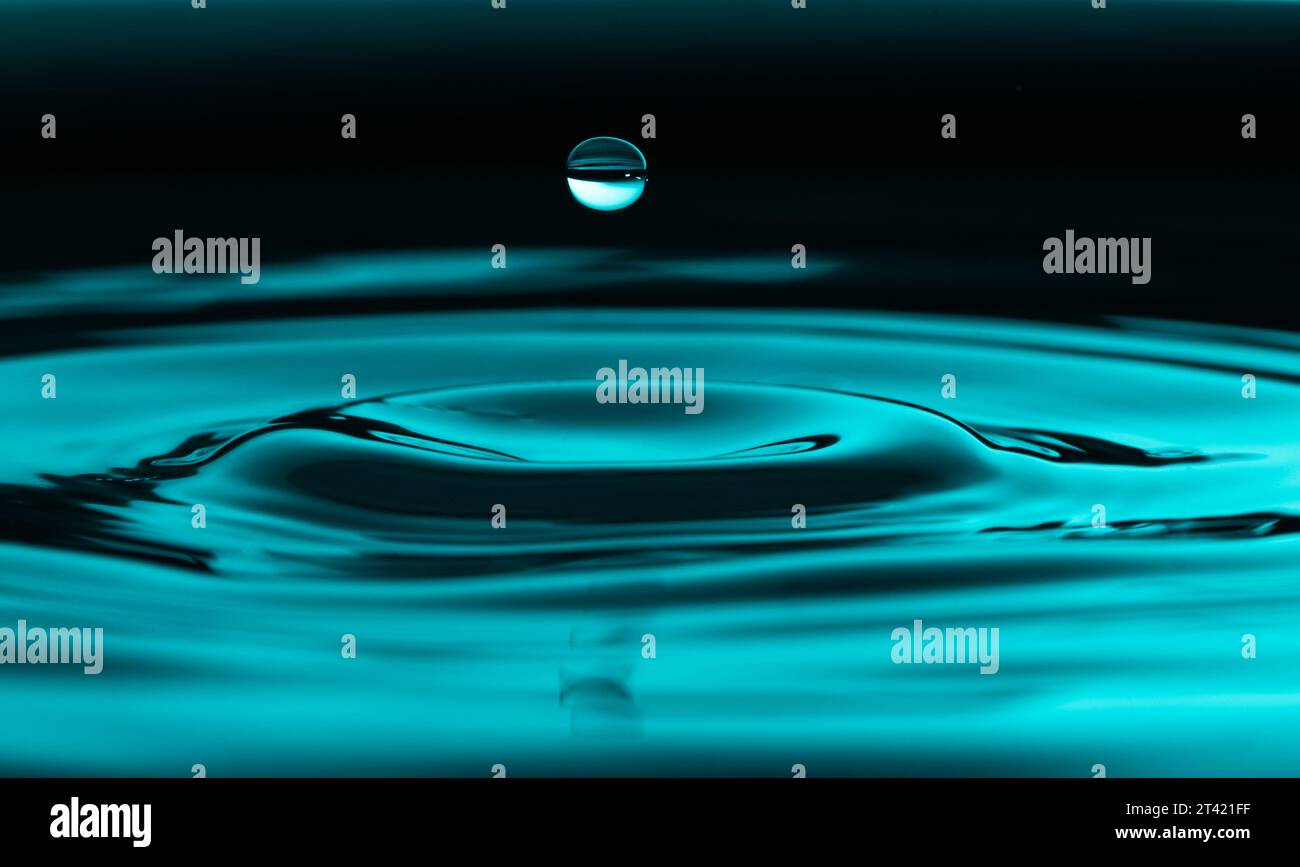 A crystal clear blue liquid with a single droplet suspended in midair ...