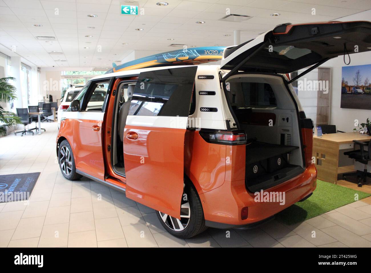 A vibrant orange van with a surfboard propped in its open door, ready ...