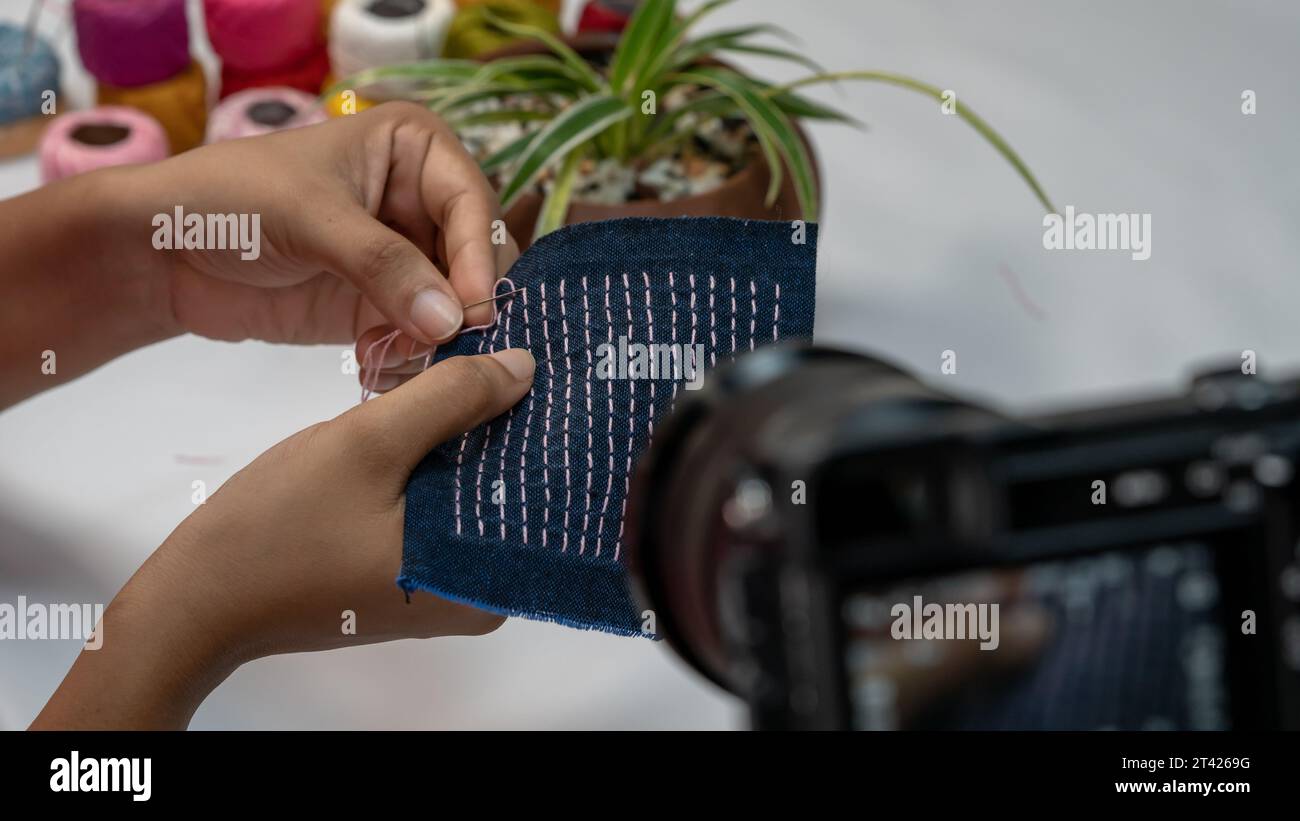 Close-up of a tailor's hand sews a piece of fabric while recording a ...