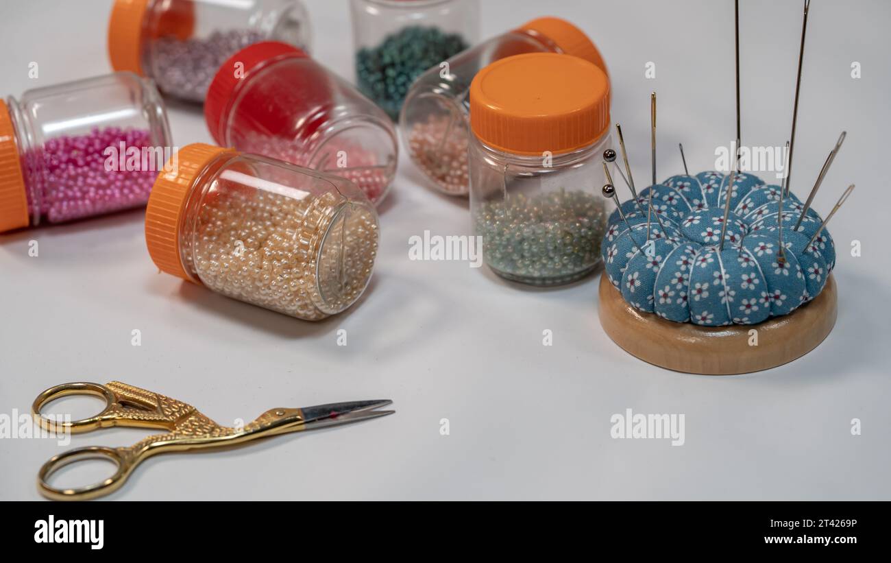 Beads and needle on pin cushion for sewing on a white background close ...